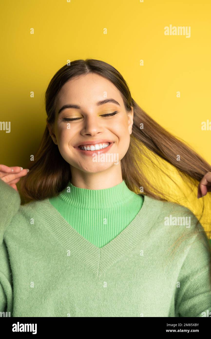 Cheerful teenager in jumper touching hair on yellow background Stock ...