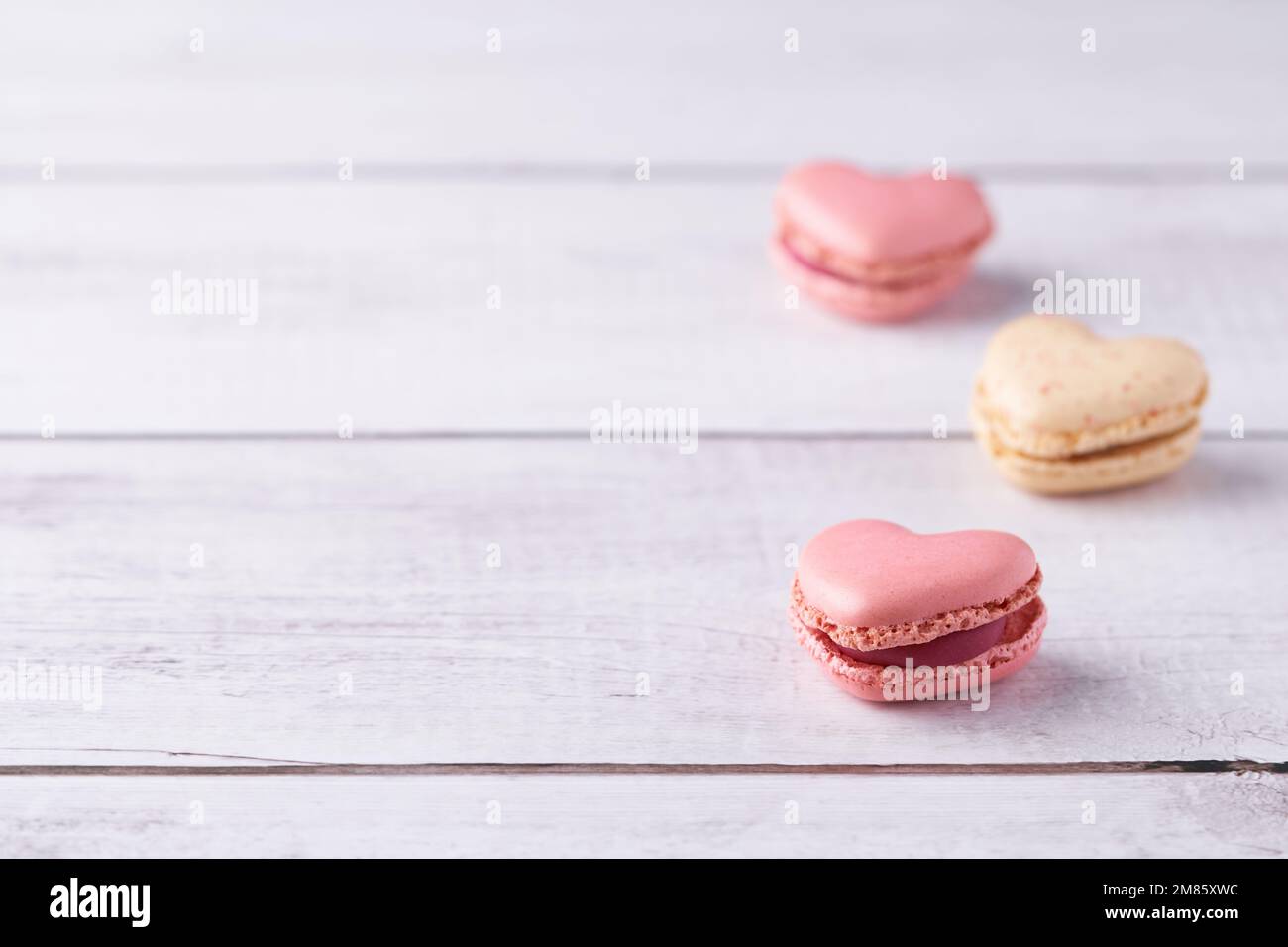 Three heart shaped, cream filled French Macaroons on white wooden ...