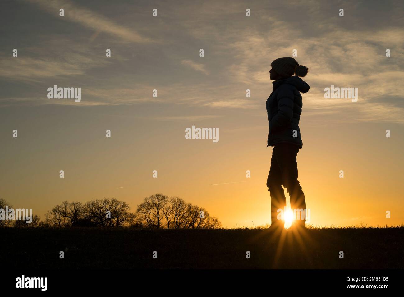 A sunburst breaks through the silhouette of an isolated woman, dressed ...