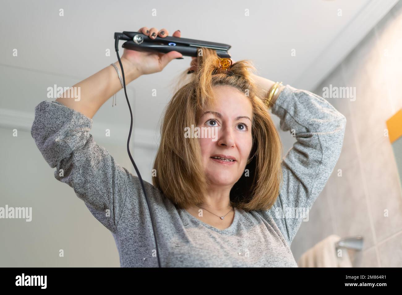 Mature white woman fixing her hair in front of the mirror with a hair ...