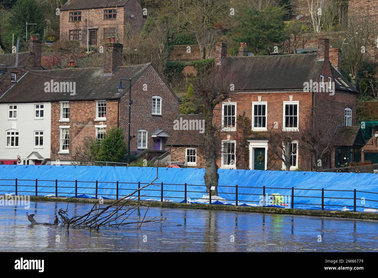 A tree branch drifts down the swollen River Severn, as flood defenses ...