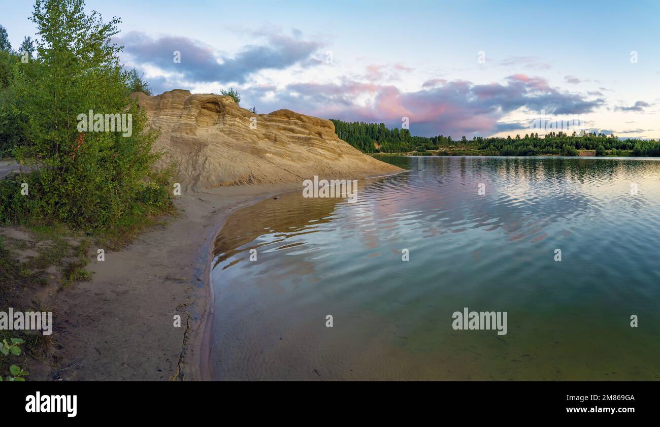 A high cliff on the shore of a lake with colorful clouds in the sky at ...