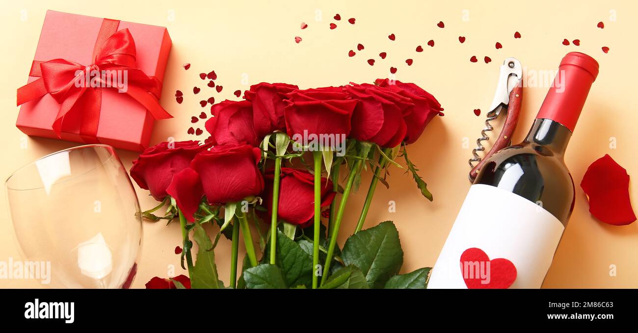 Bottle of wine, red rose flowers, gift and glass on beige background ...