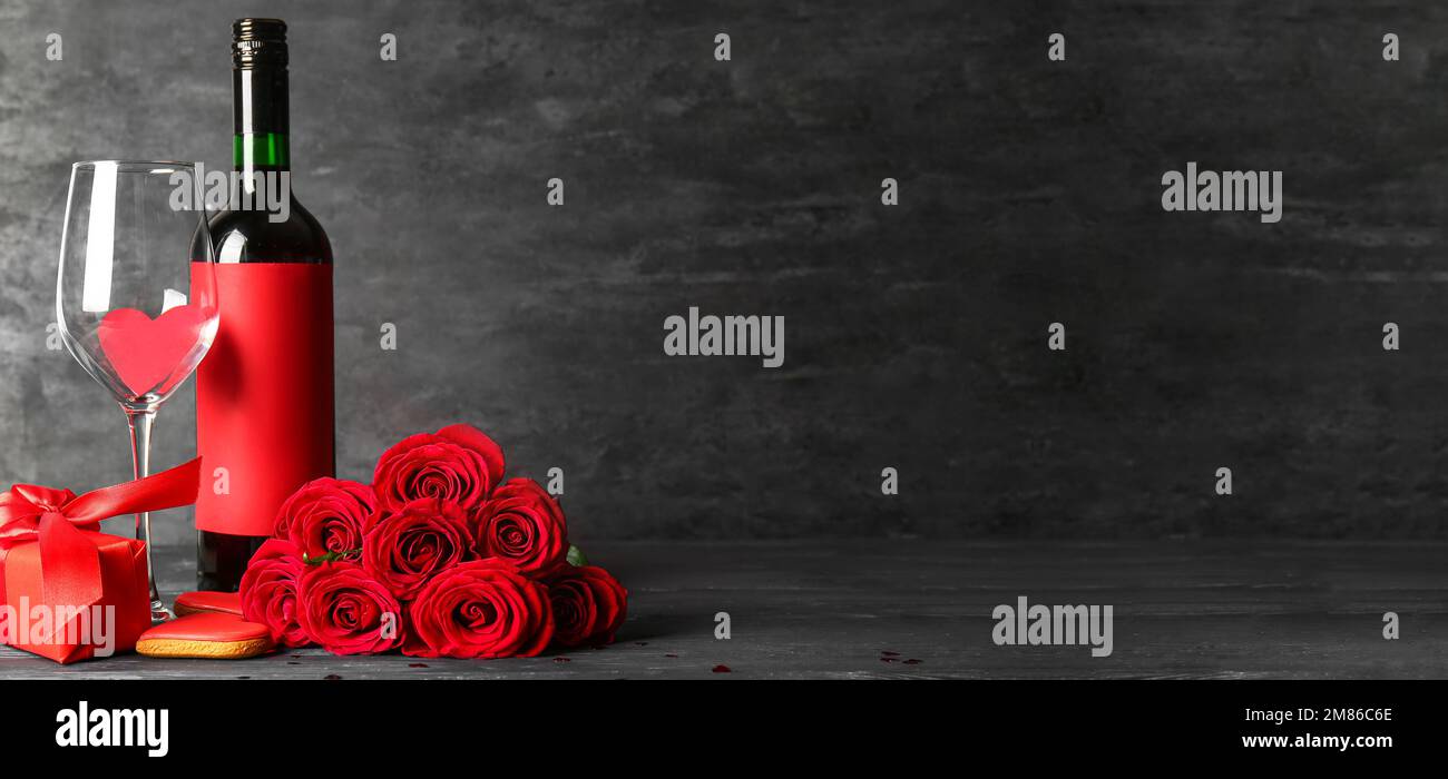 Bottle of wine, rose flowers, glass and gift on dark background with ...