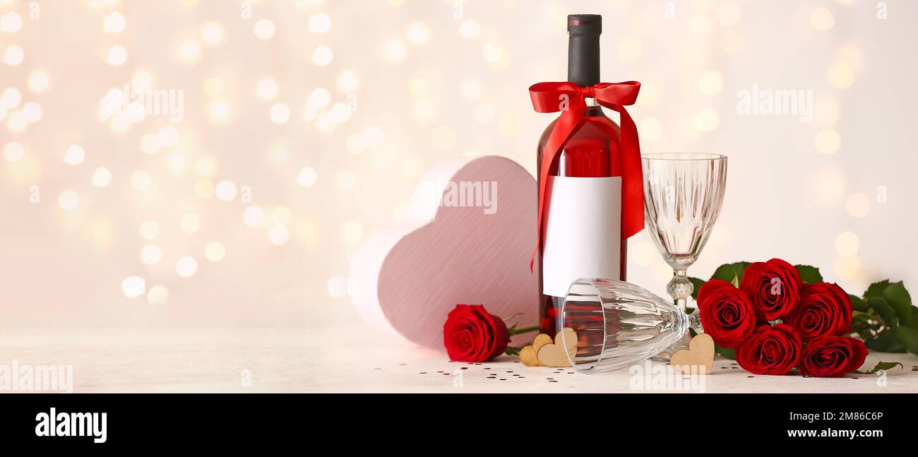 Bottle of wine, red rose flowers, gift and glasses on light background ...