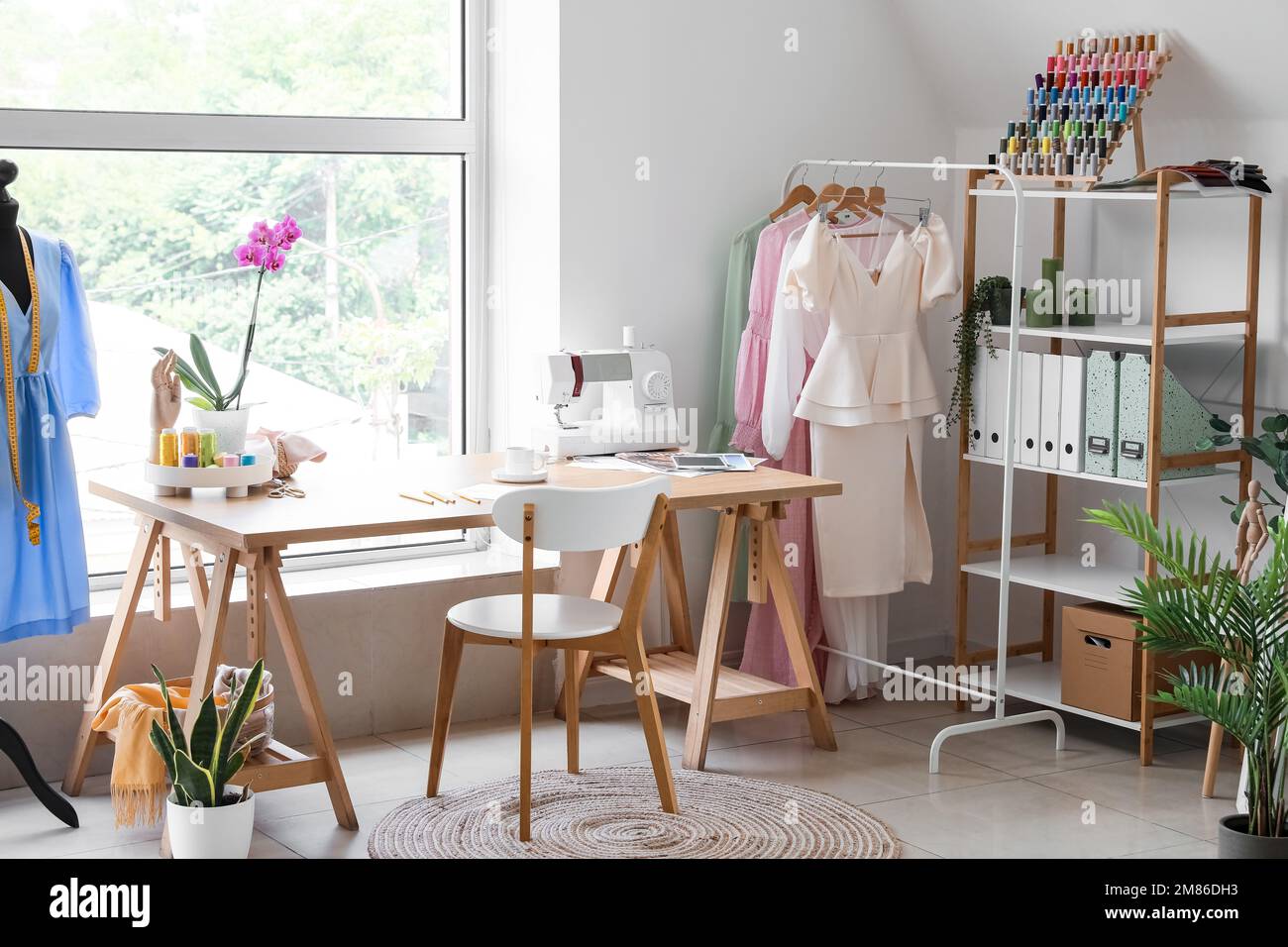 Interior of light atelier with tailor's workplace, clothes and shelving ...