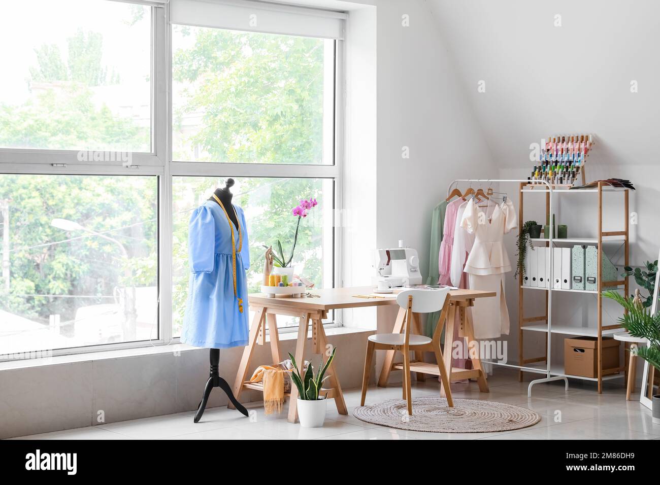 Interior of light atelier with tailor's workplace, clothes and shelving ...