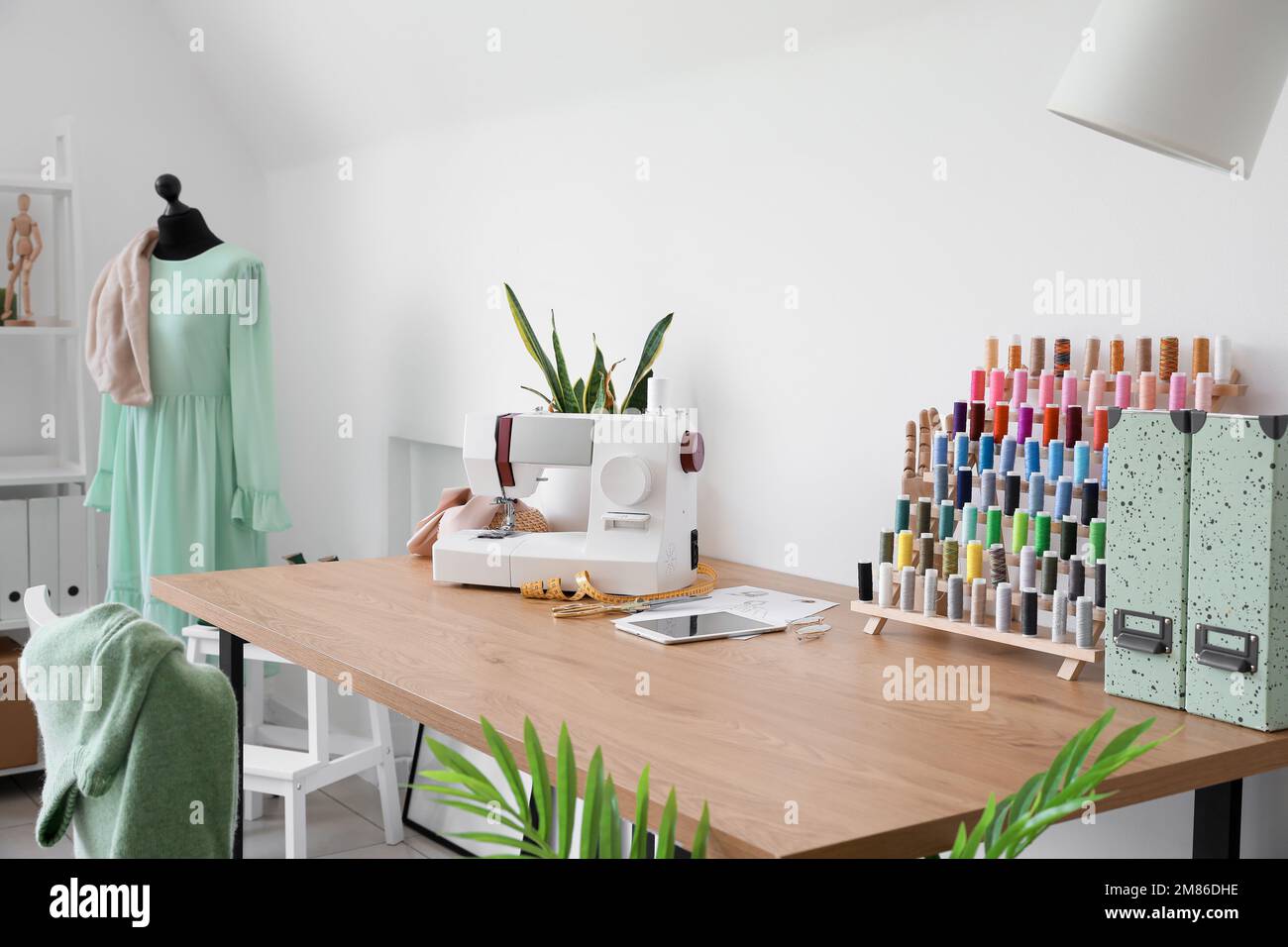 Tailor's workplace with sewing machine and thread pools near light wall ...