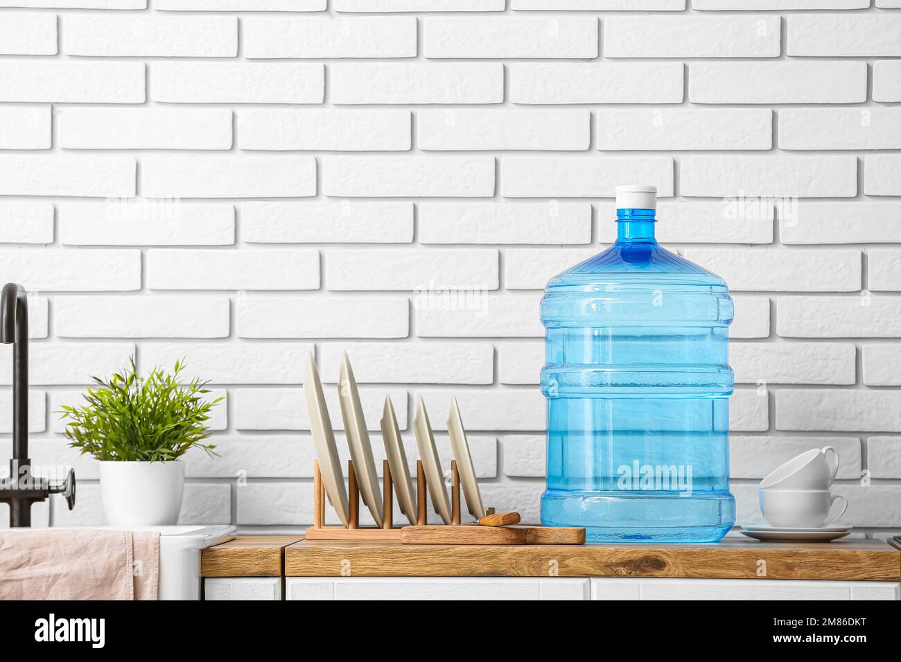 Bottle of clean water, plates and cups on kitchen counter near white ...