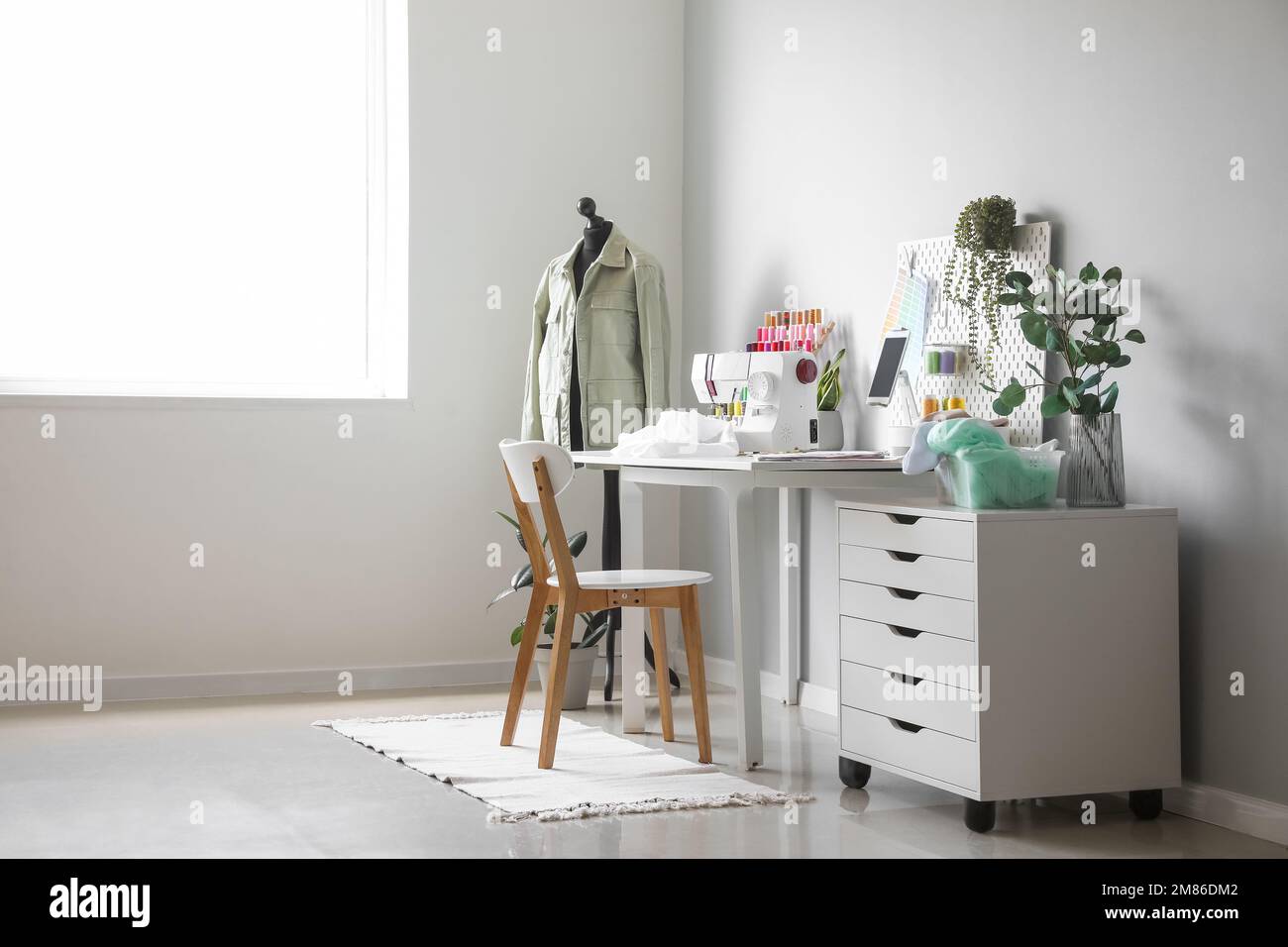Tailor's workplace with sewing machine, pegboard and tablet computer in ...