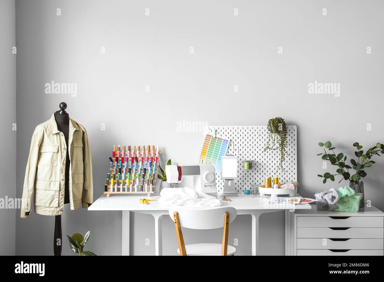 Tailor's workplace with sewing machine, pegboard and tablet computer in ...