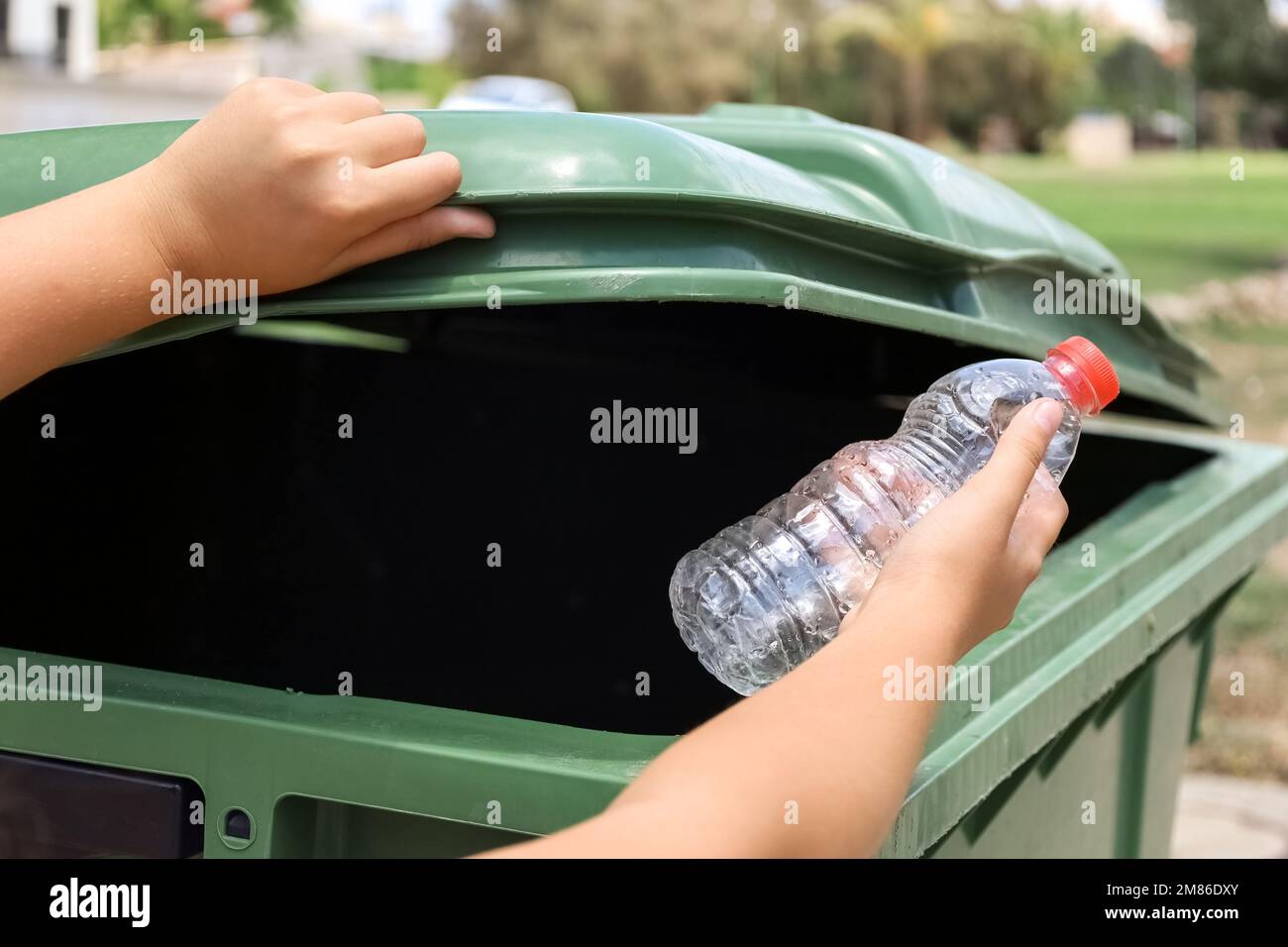 Child throwing plastic bottle into garbage container outdoors, closeup ...
