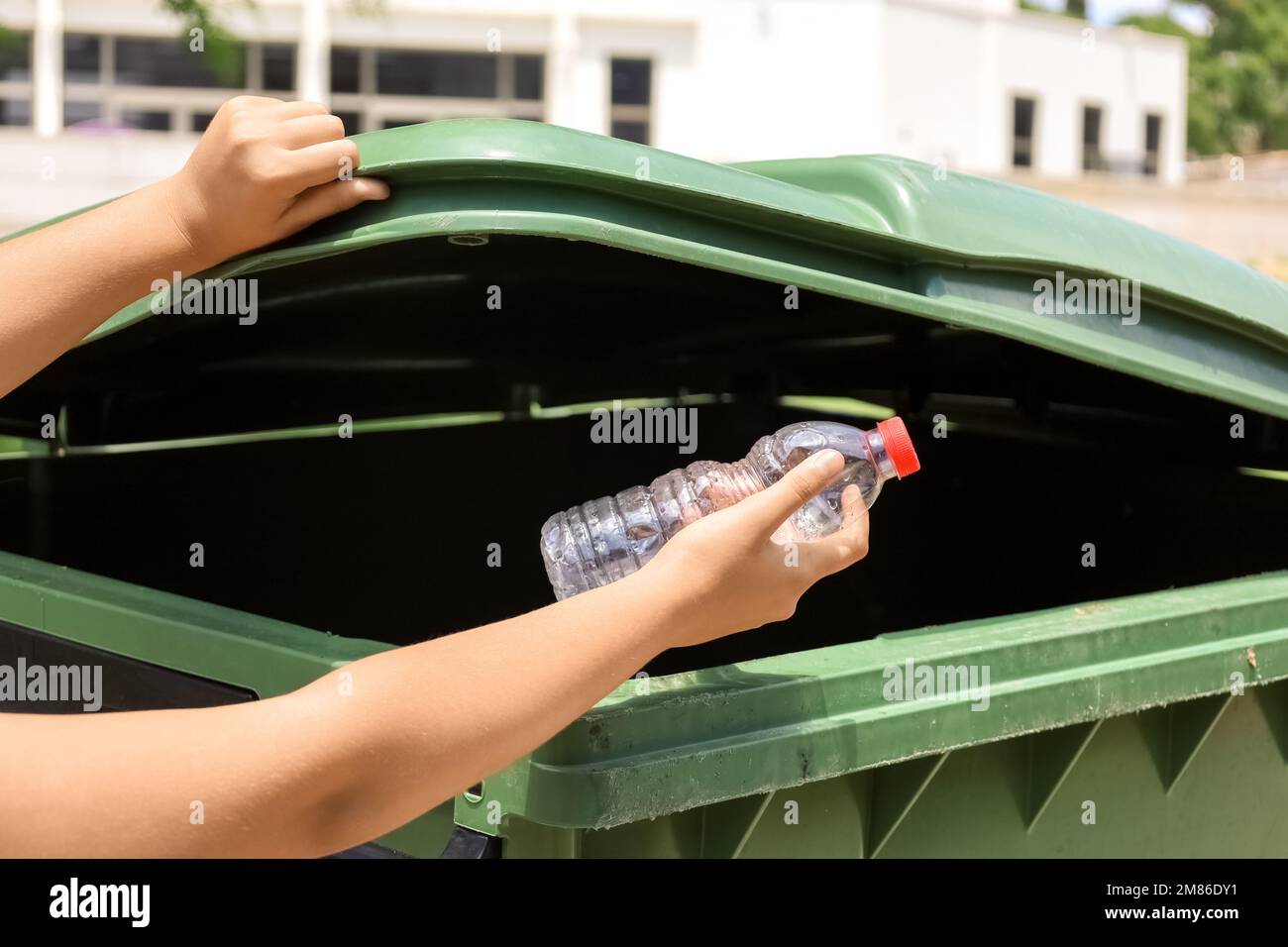 Child throwing plastic bottle into garbage container outdoors, closeup ...
