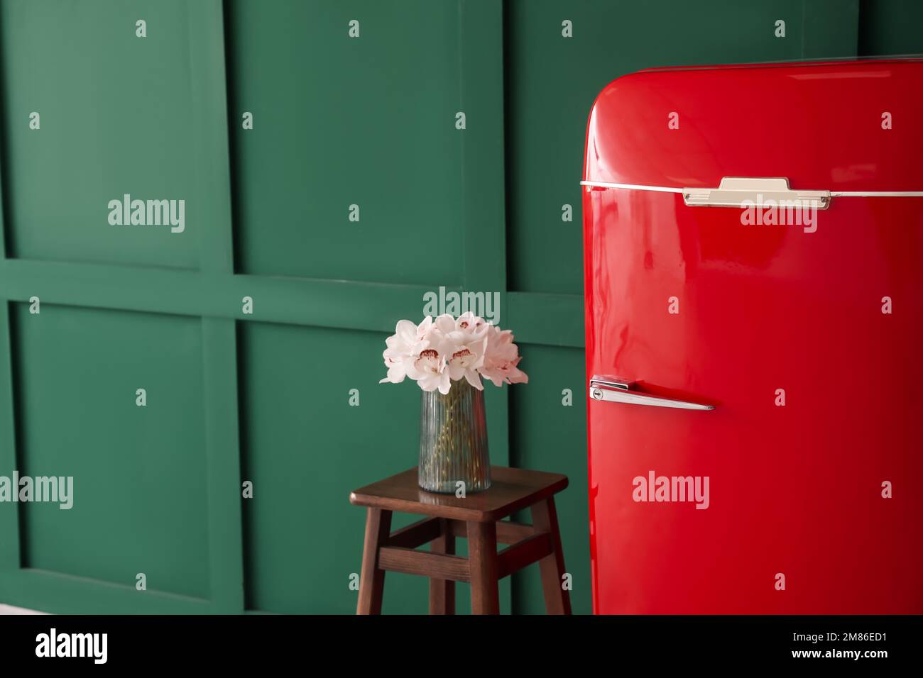Stylish retro fridge and stool with flowers in vase near green wall ...