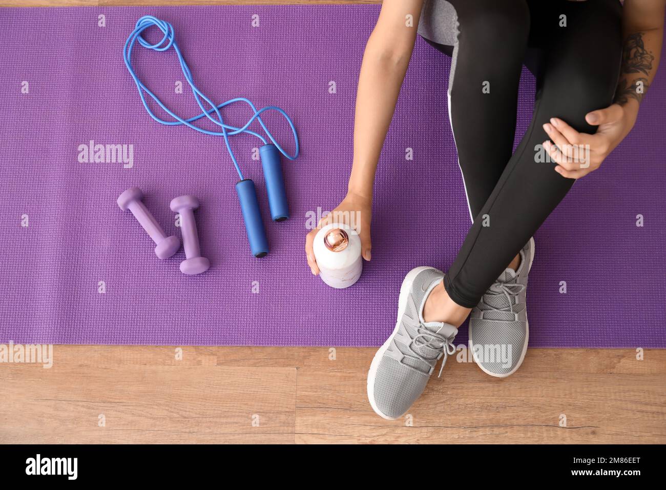 Woman with sports water bottle and equipment sitting on mat in gym ...