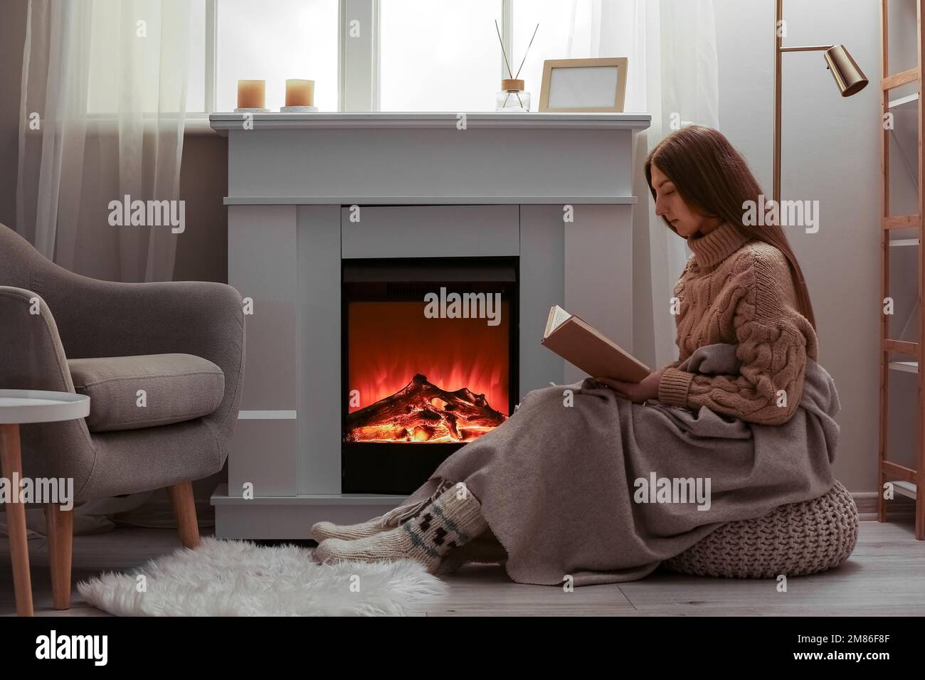 Young woman reading book near fireplace in living room Stock Photo - Alamy