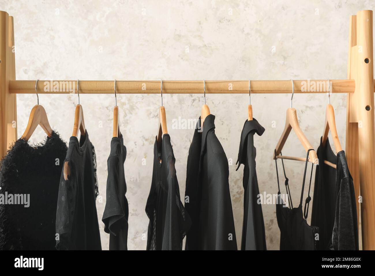 Rack with black female clothes near light wall Stock Photo - Alamy