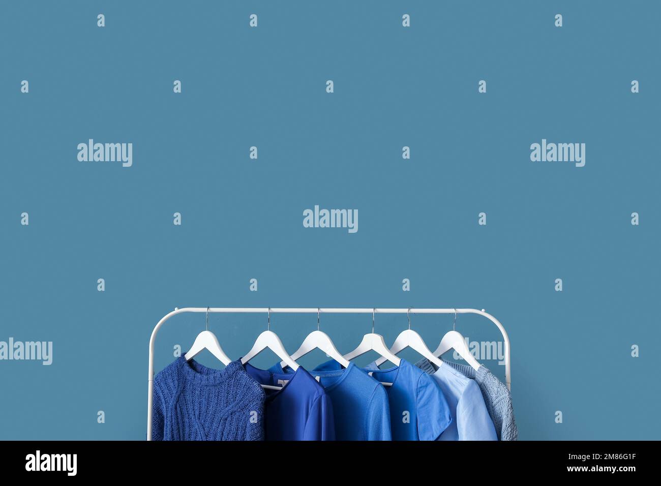Rack with blue clothes near color wall Stock Photo - Alamy