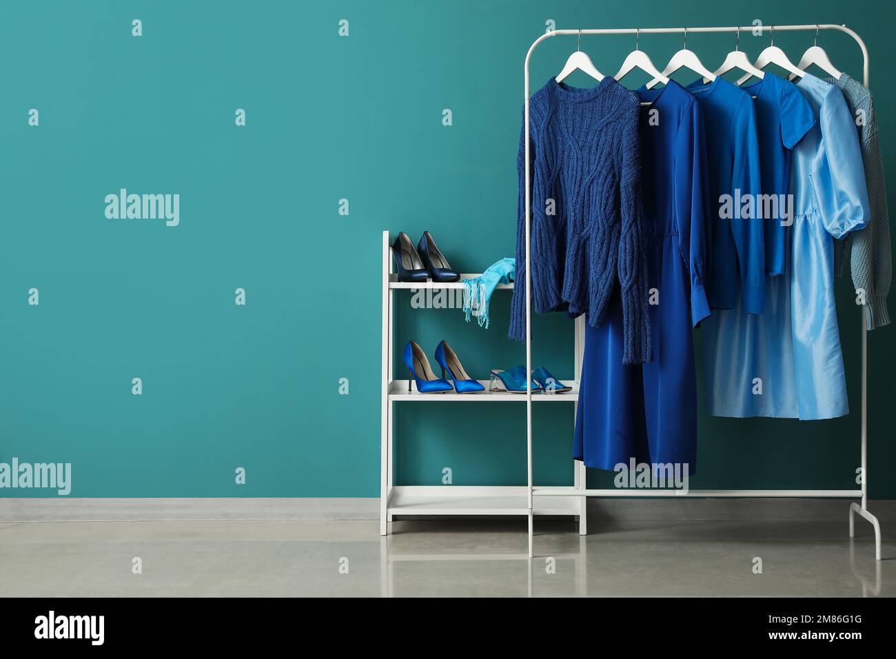 Rack with blue clothes and shoe stand near color wall Stock Photo - Alamy