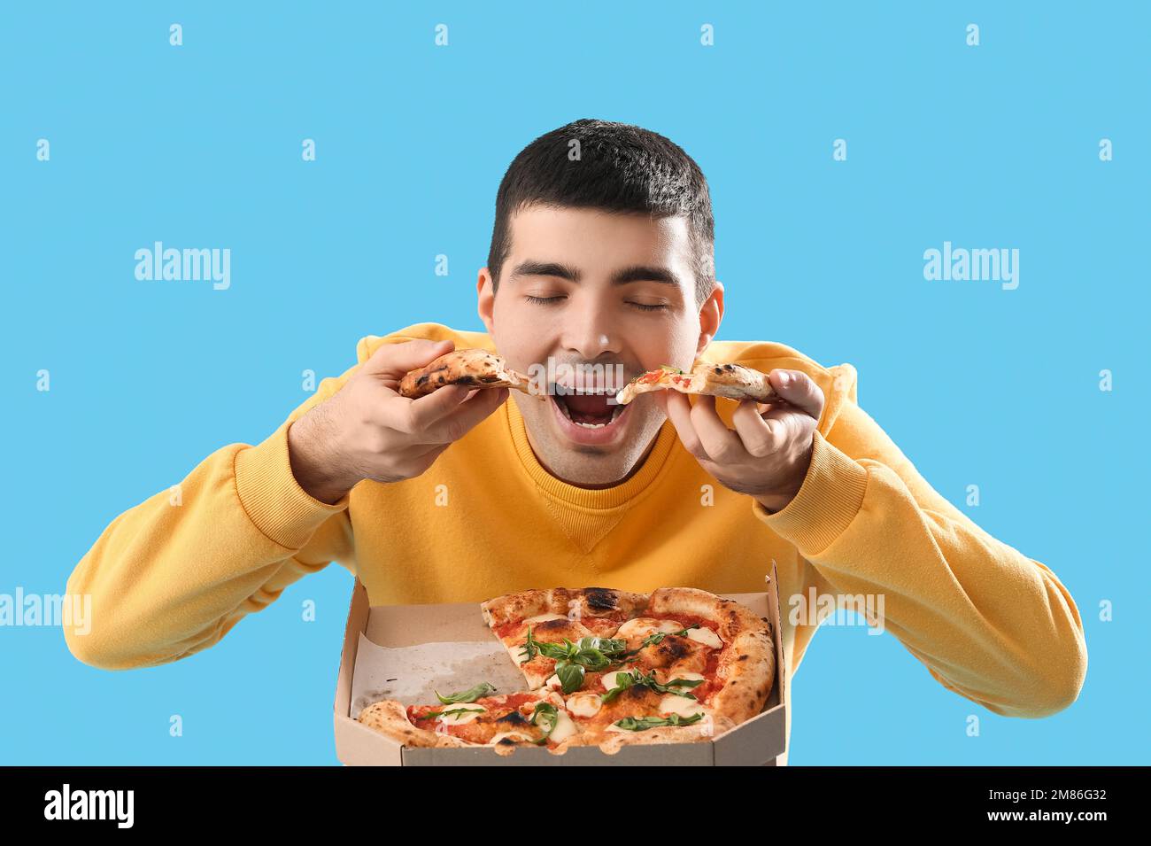 Young man eating tasty pizza on blue background Stock Photo - Alamy