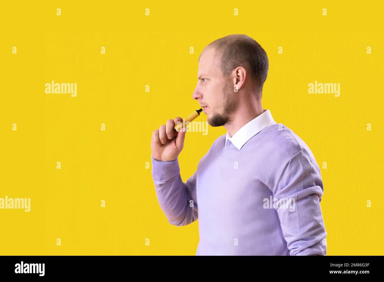 Young man smoking disposable electronic cigarette on yellow background ...