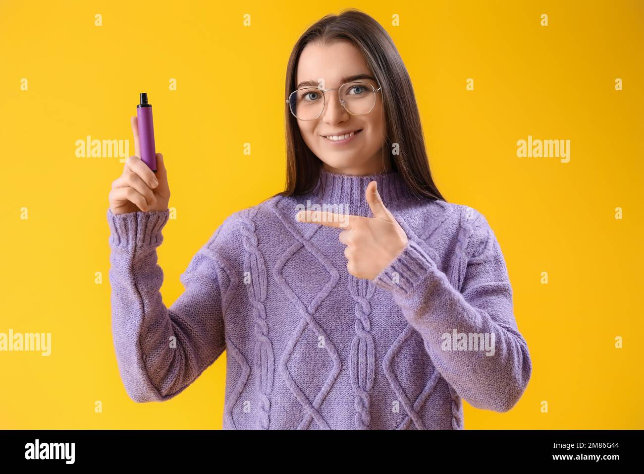 Young woman pointing at disposable electronic cigarette on yellow ...