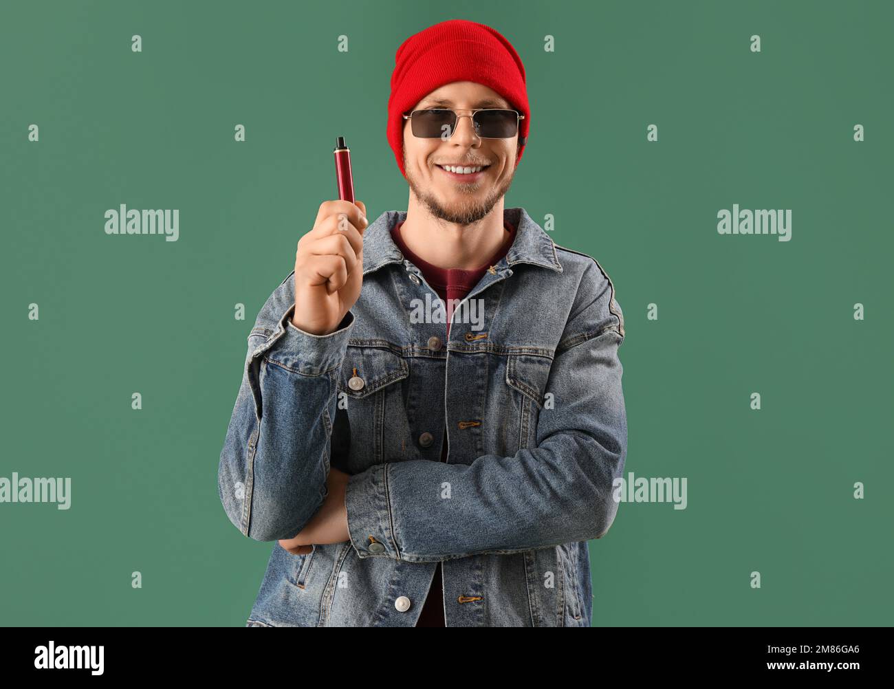 Stylish young man with disposable electronic cigarette on green ...