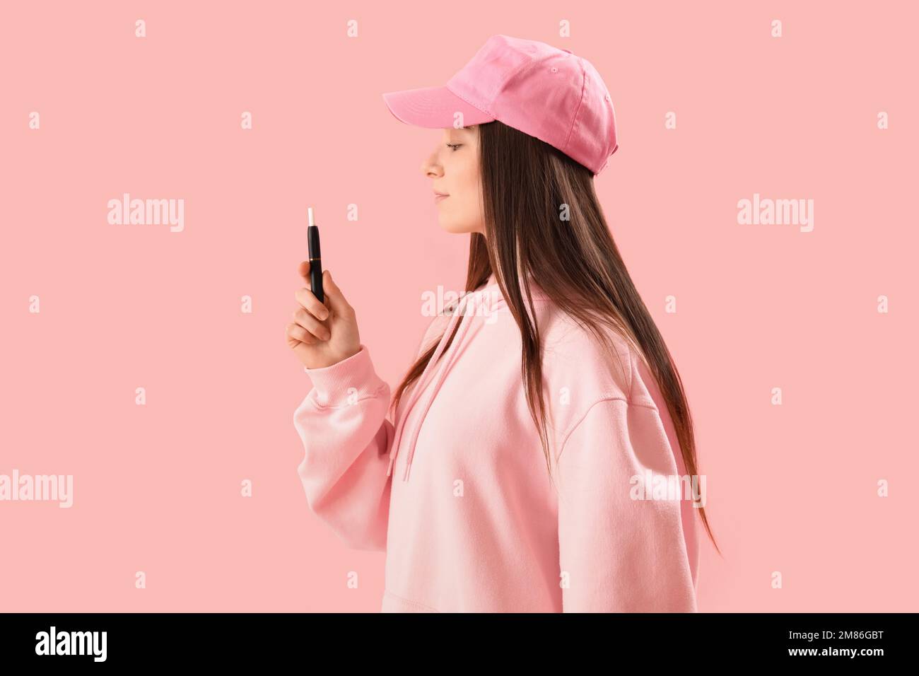 Young woman in cap with disposable electronic cigarette on pink ...