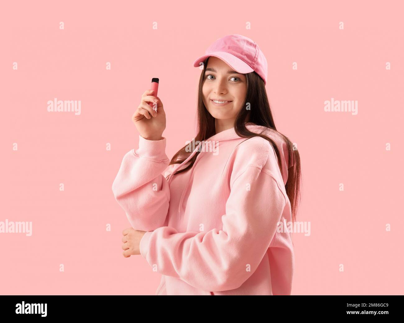 Young woman in cap with disposable electronic cigarette on pink ...