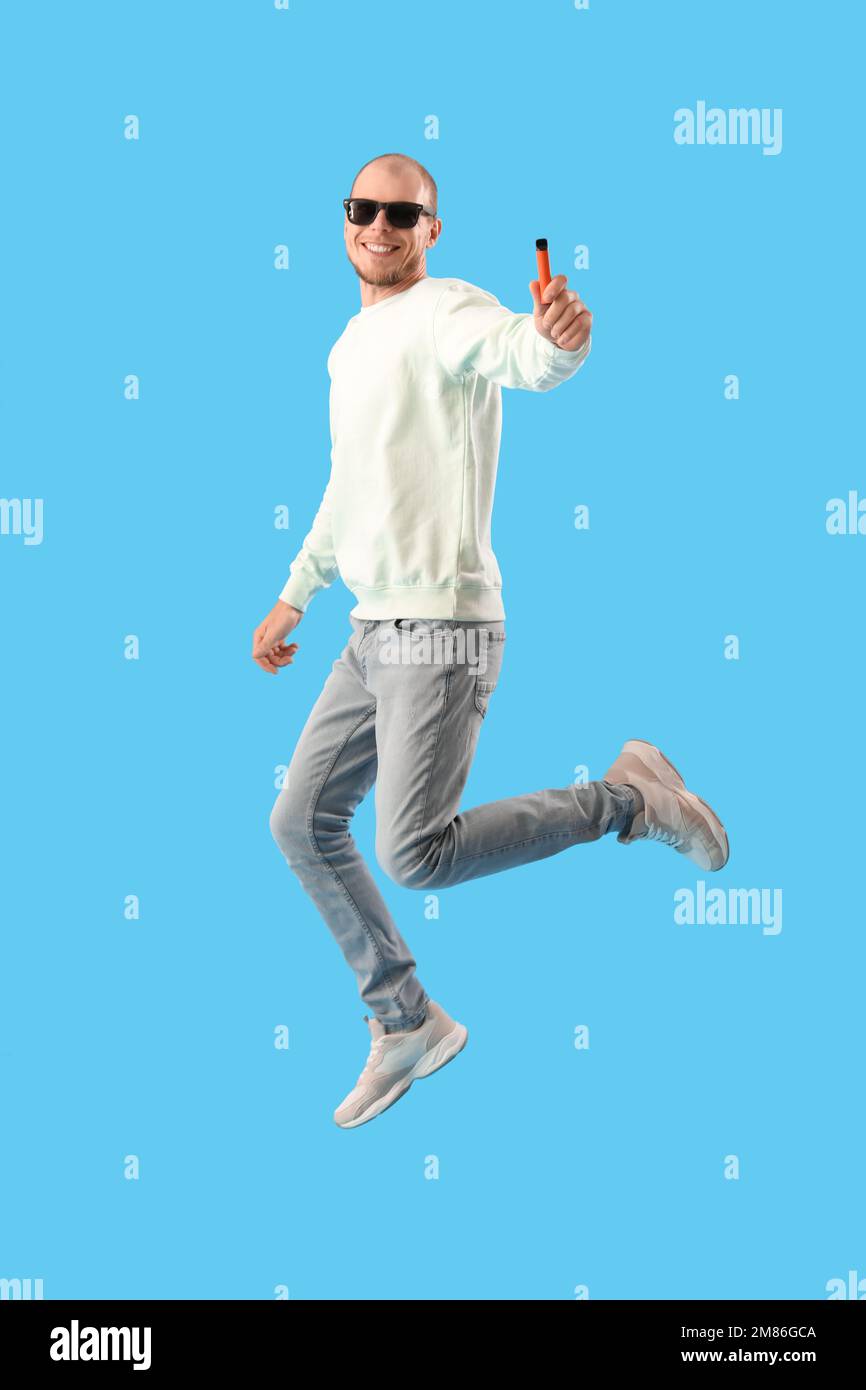 Young man in sunglasses with disposable electronic cigarette jumping on ...