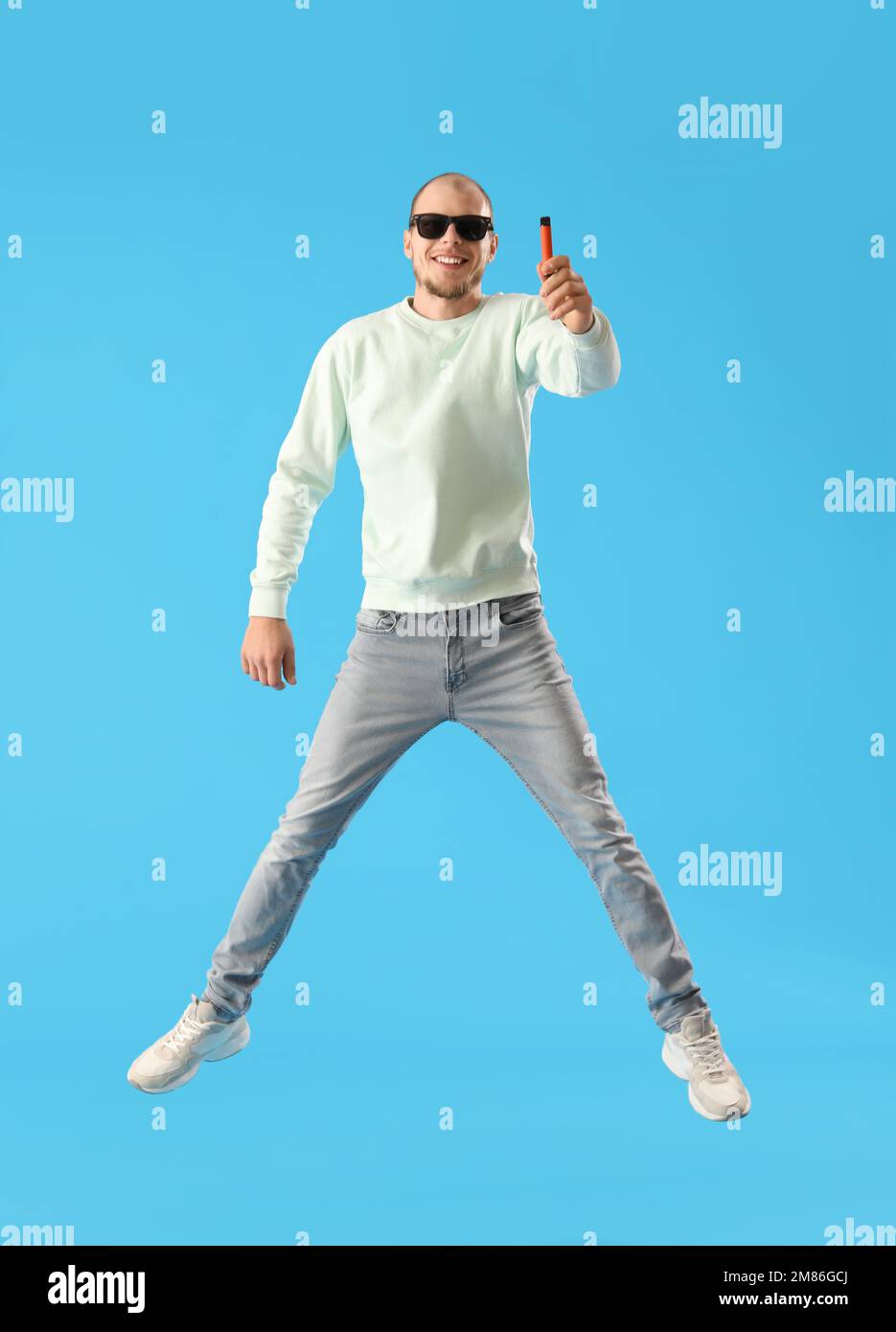 Young man in sunglasses with disposable electronic cigarette jumping on ...