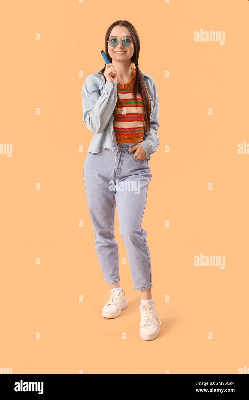 Young woman in sunglasses with disposable electronic cigarette on beige ...