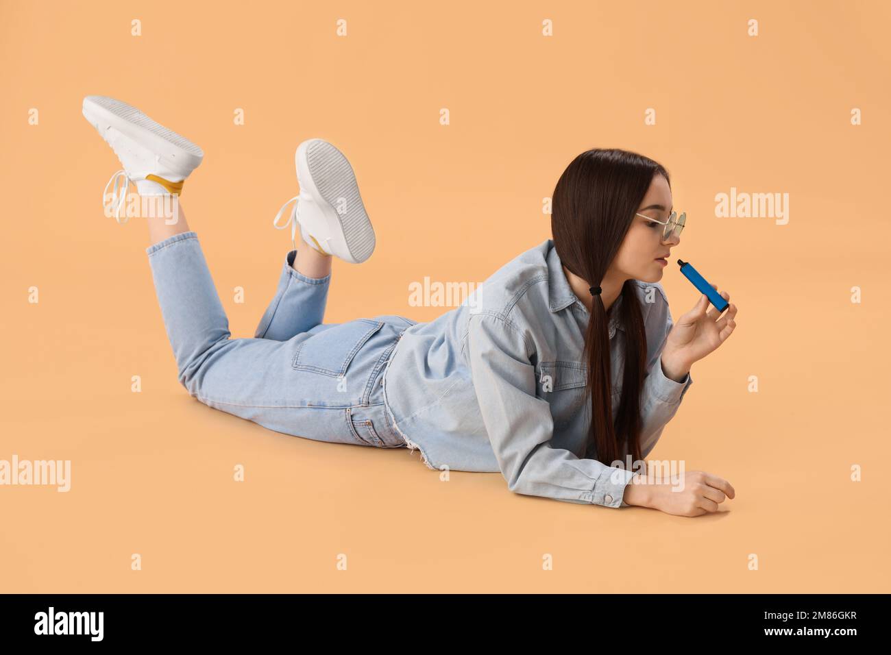 Young woman in sunglasses with disposable electronic cigarette lying on ...
