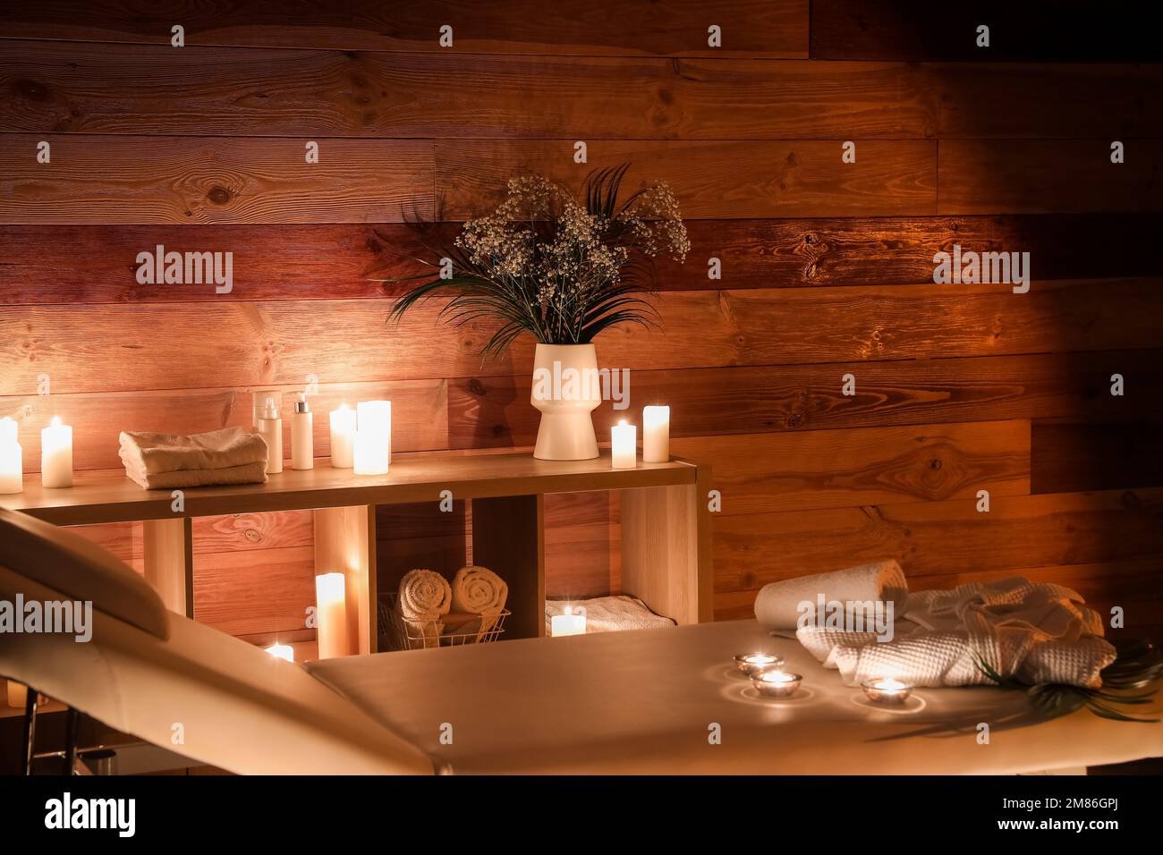 Interior of dark spa salon with couch, shelving unit and burning ...