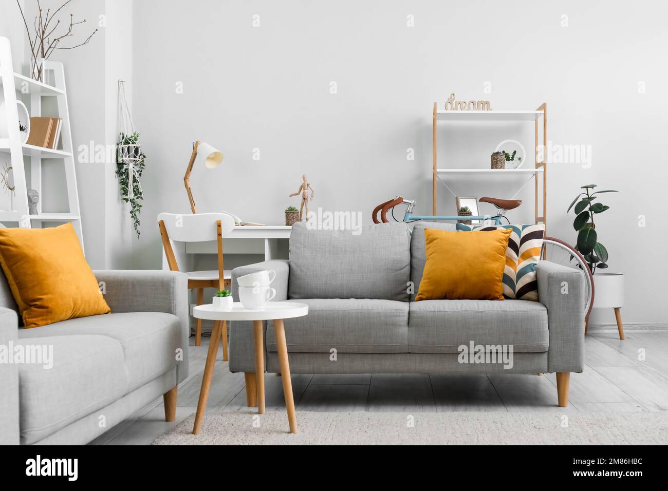 Interior of living room with grey sofas, coffee table, workplace, shelving units and bicycle ...