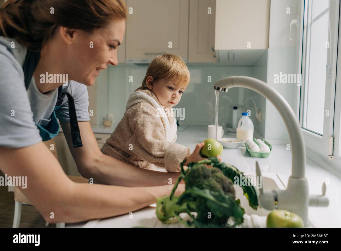 Mother and little child toddler are washing vegetables together in the ...