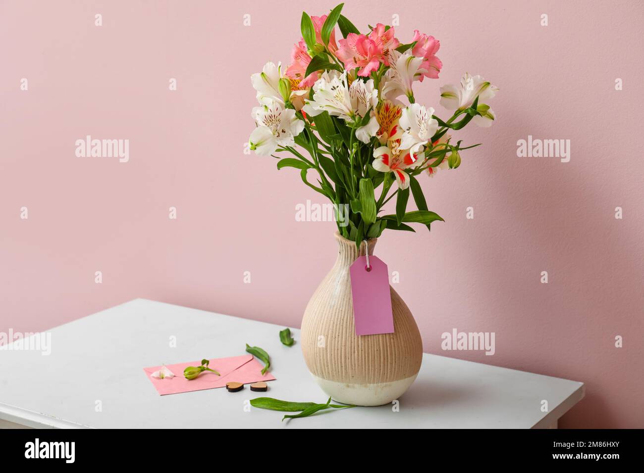 Vase with beautiful alstroemeria flowers and envelope on table near ...