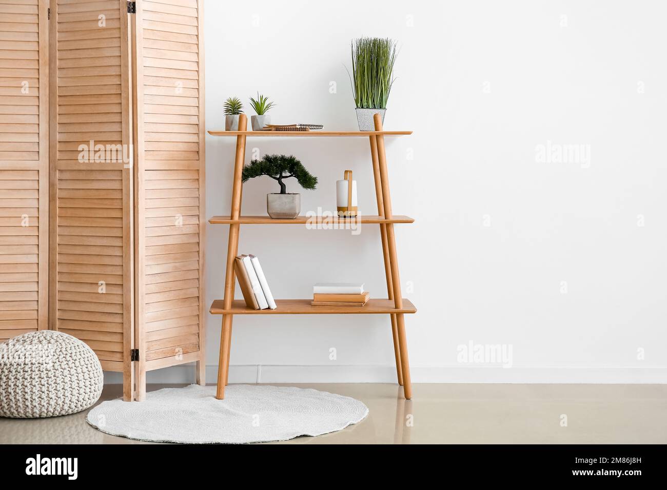 Interior of room with folding screen, shelving unit and pouf near white ...