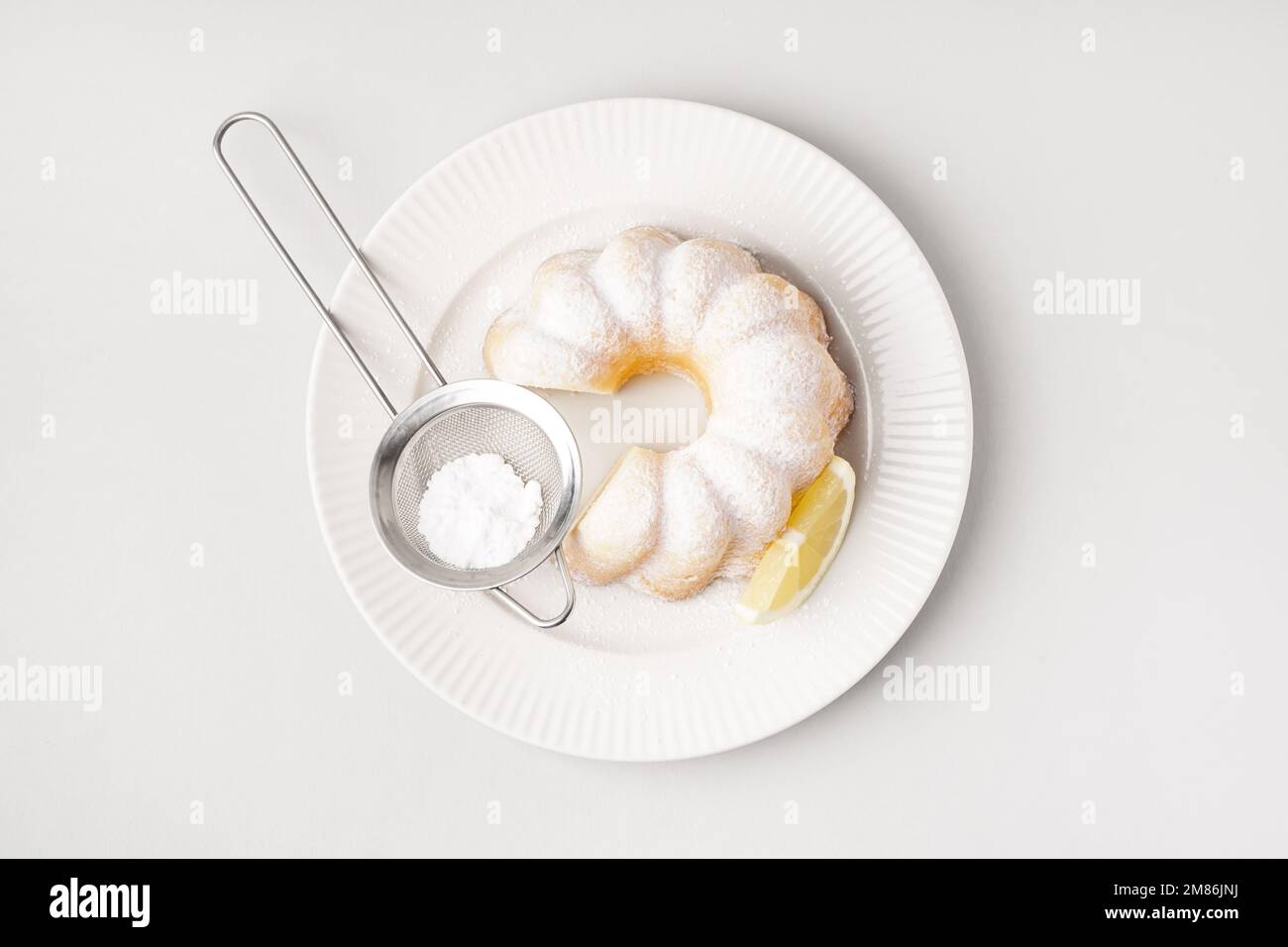 Plate with delicious cake, sieve of powdered sugar and lemon slice on ...