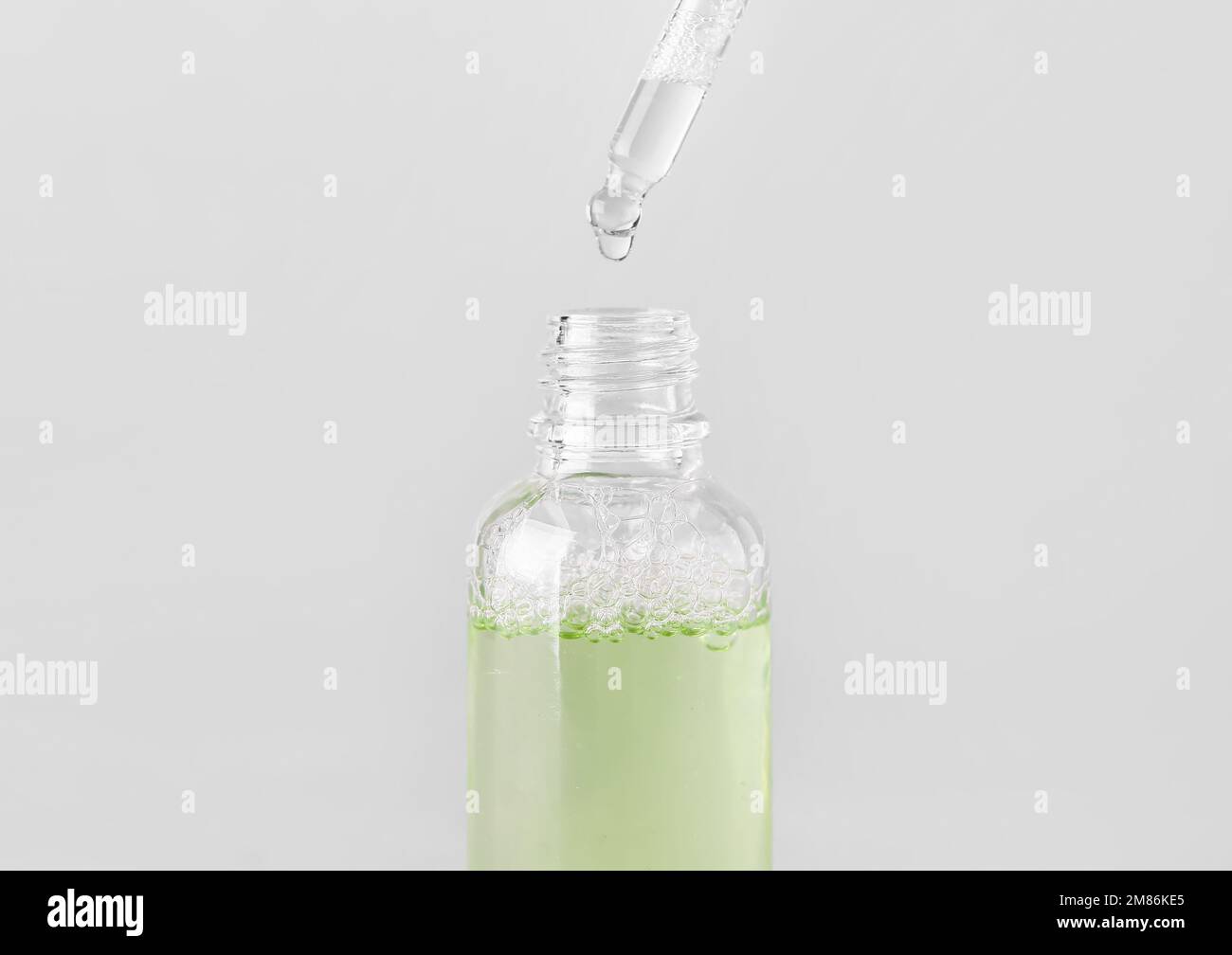 Dripping of serum from pipette into glass bottle on light background ...