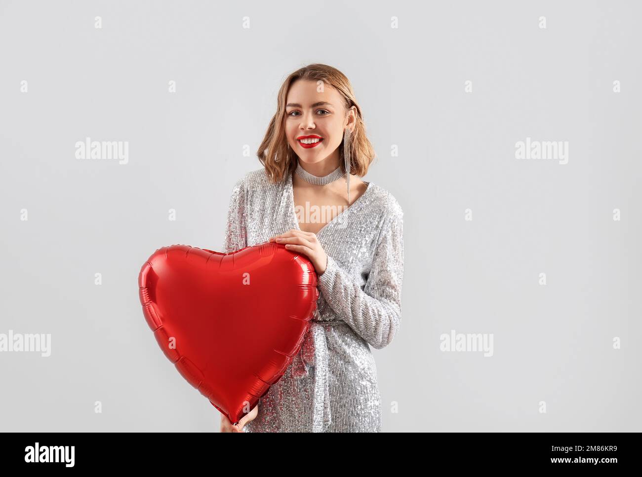 Beautiful young woman with red heart-shaped balloon on light background ...