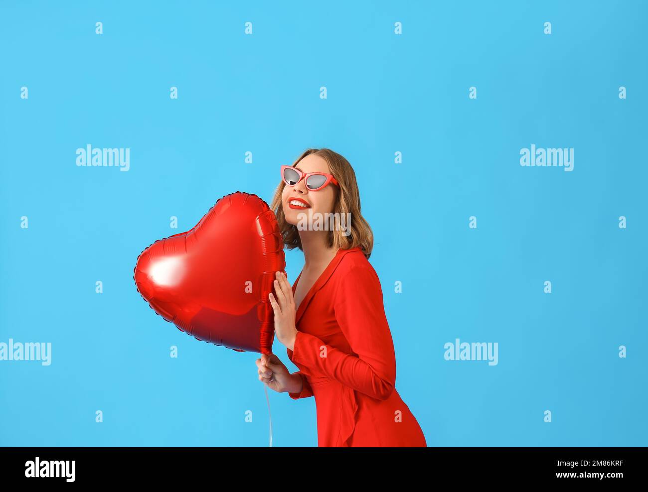 Beautiful young woman with red heart-shaped balloon on blue background ...