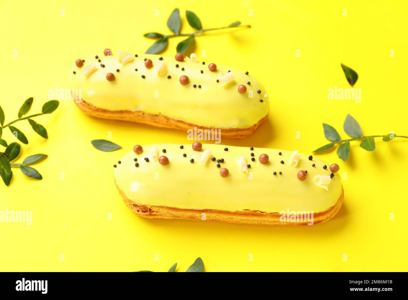 Delicious glazed eclairs and eucalyptus on yellow background Stock ...