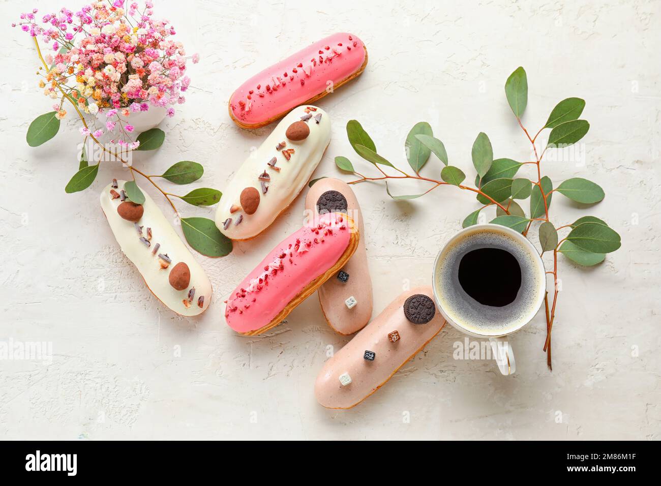 Delicious glazed eclairs, cup of coffee and eucalyptus on light ...