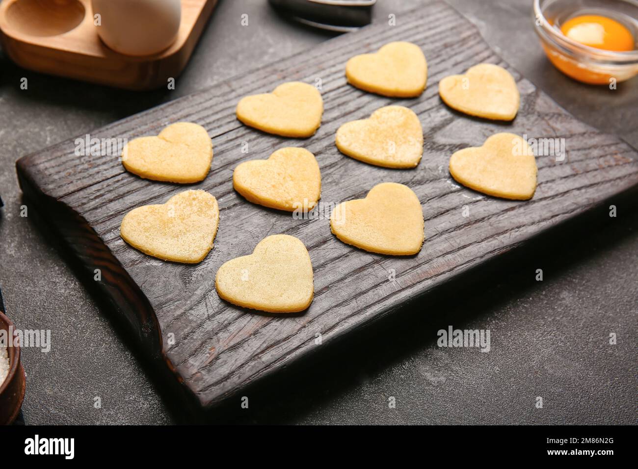 Wooden board with raw heart shaped cookies on dark background, closeup ...