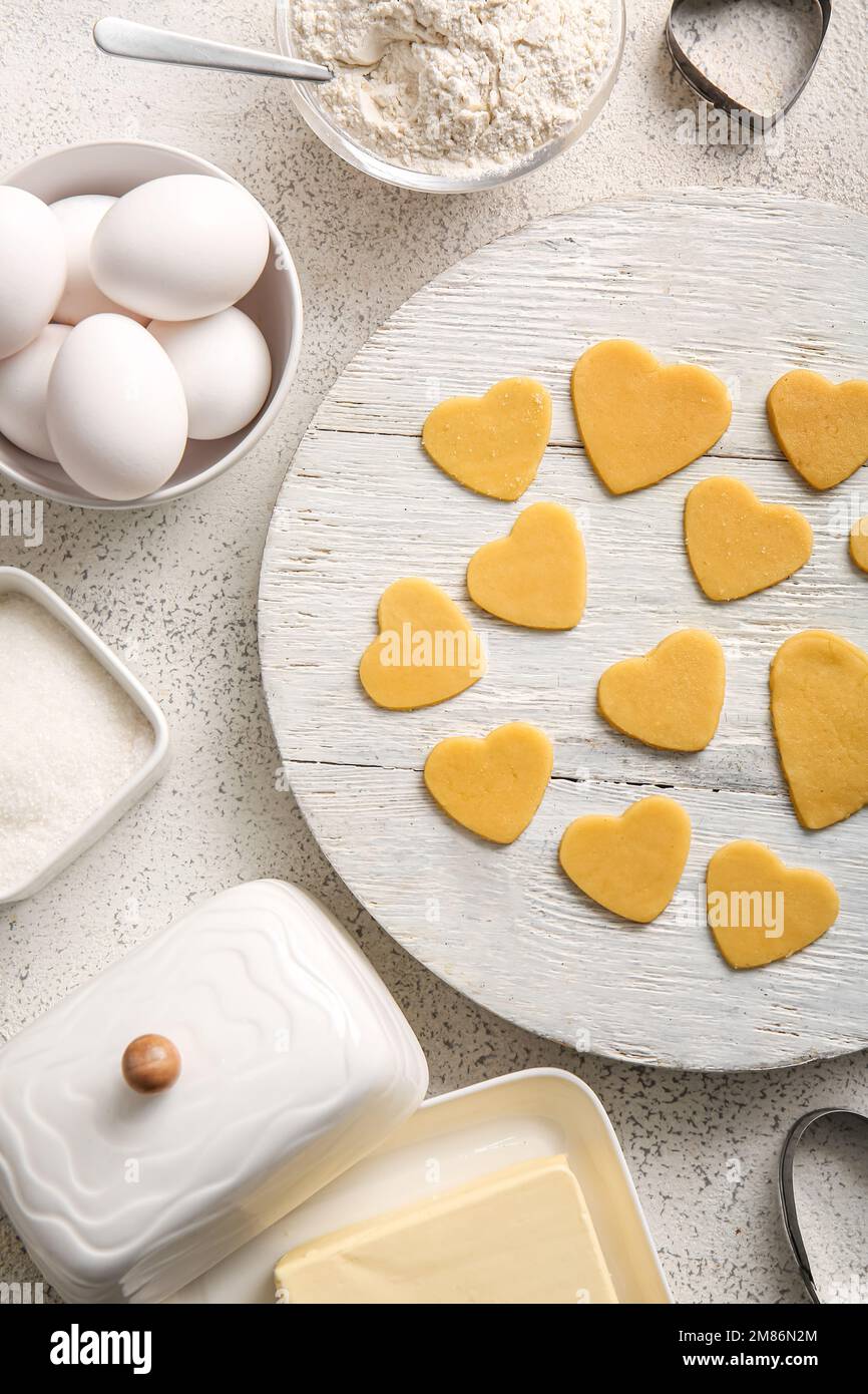 Wooden board with raw heart shaped cookies and ingredients on light ...