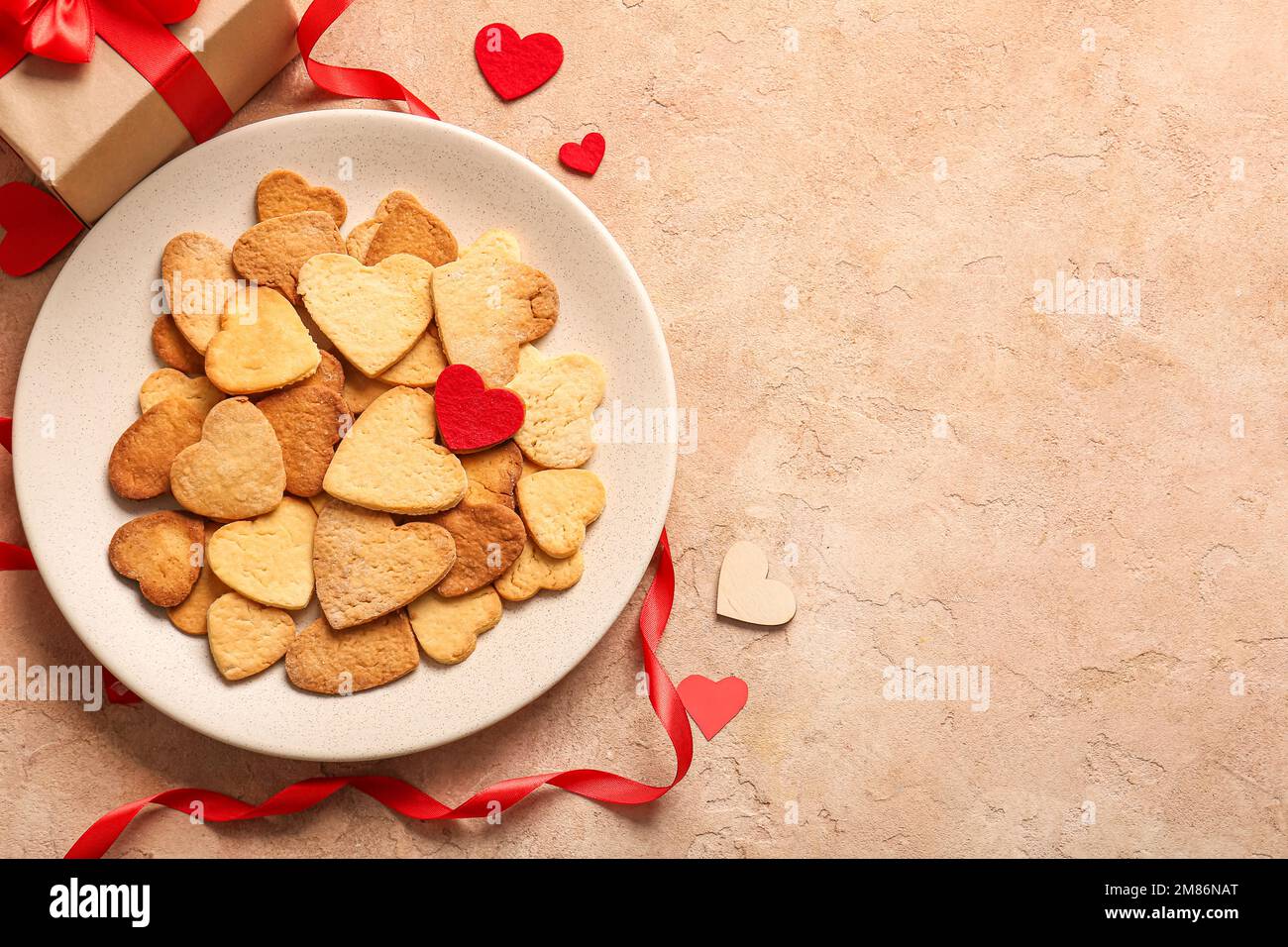 Plate with sweet heart shaped cookies and gift on color background ...