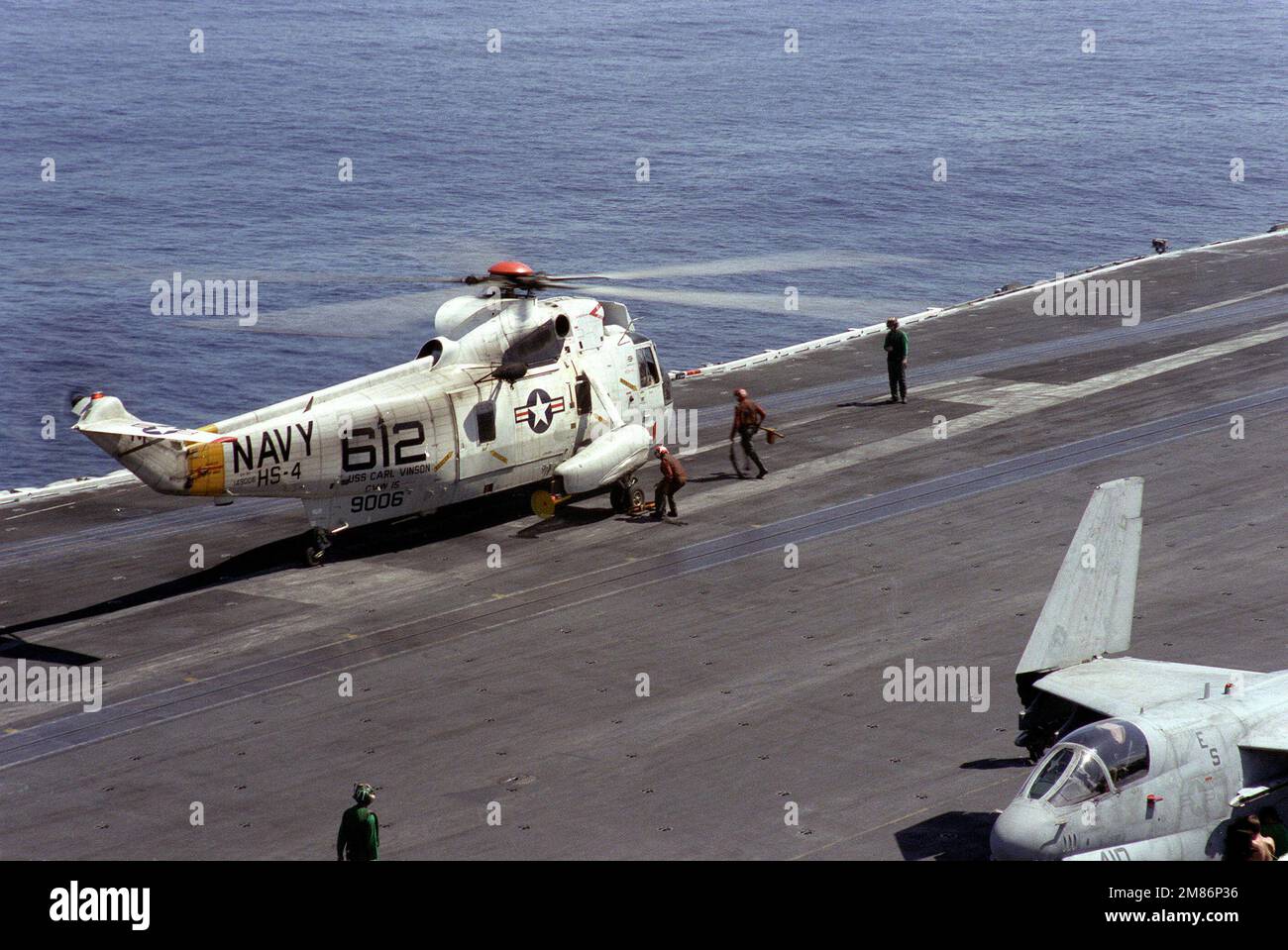 Flight deck crewmen place chocks on the landing gear of a Helicopter ...