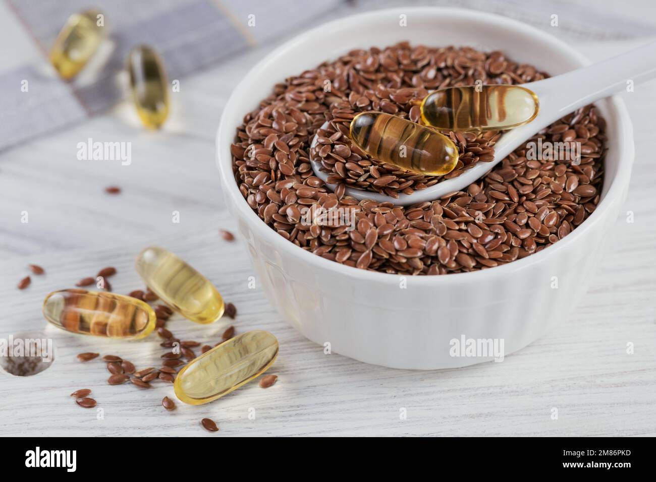 Brown flax seed or linseed in small bowl and gelatin capsules with linen seed oil on a white ...