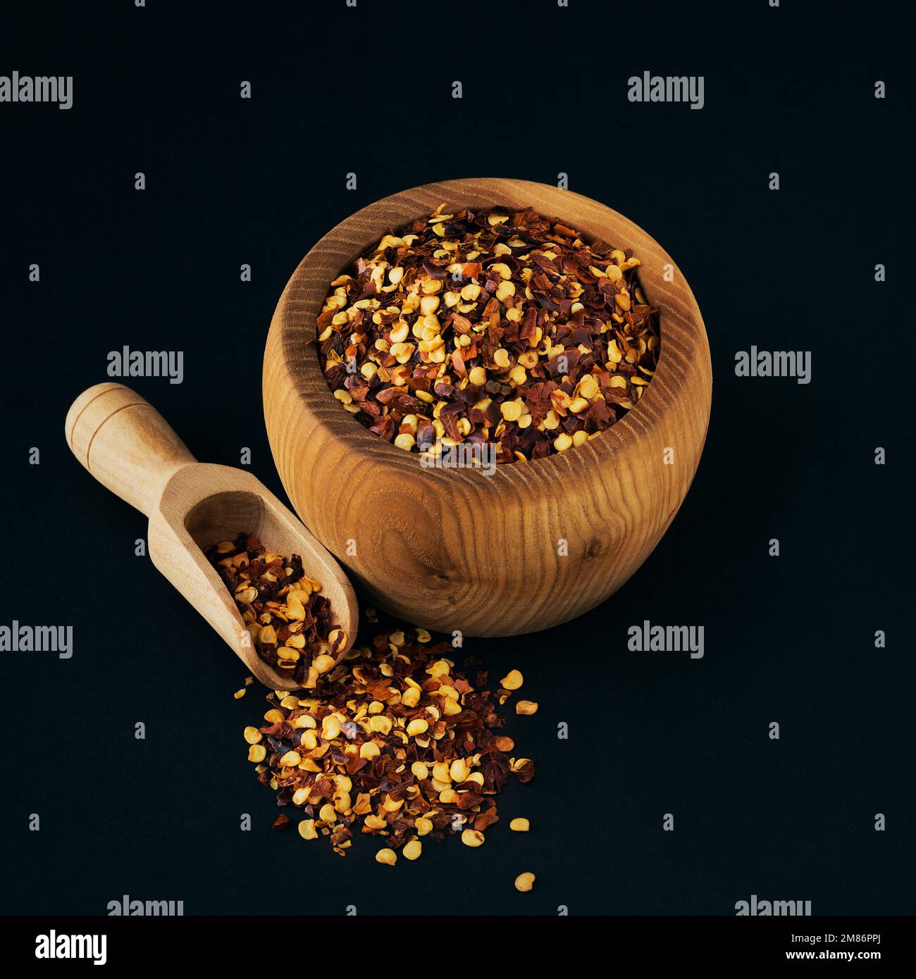 Wooden bowl of crushed red cayenne pepper, dried chili flakes and seeds ...